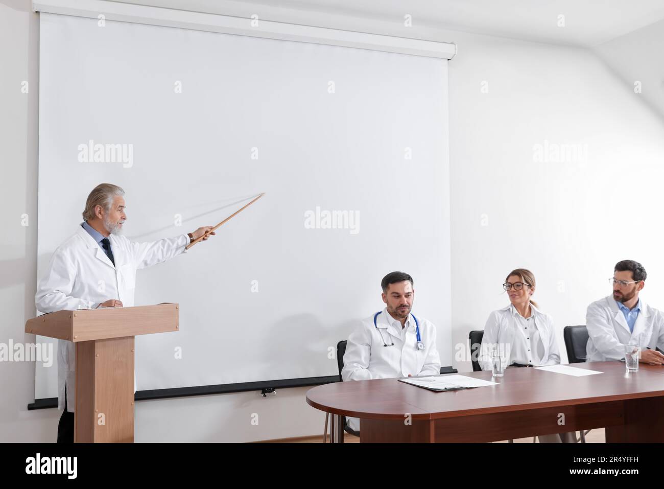 Senior doctor giving lecture in conference room with projection screen ...