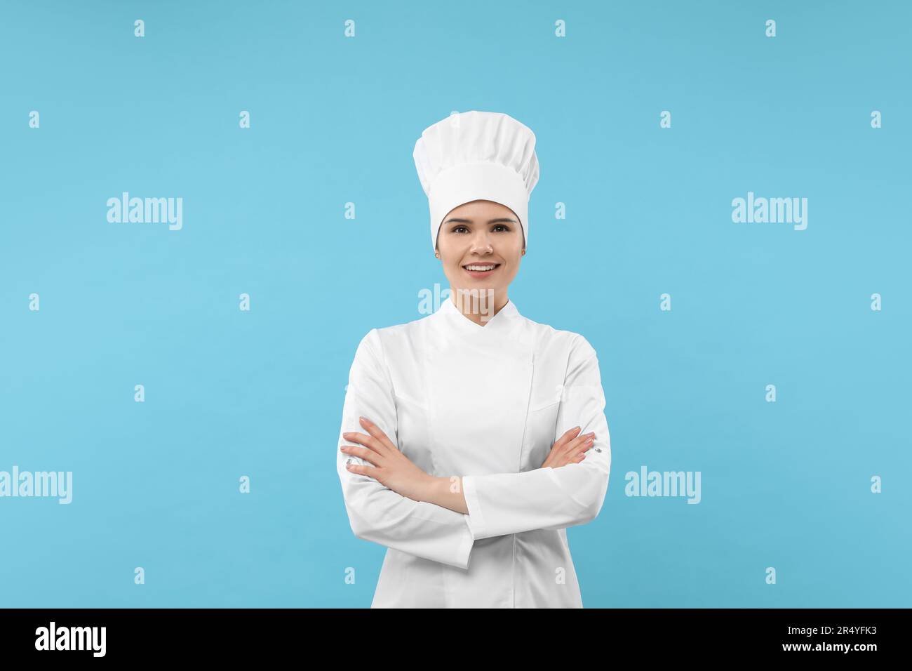 Happy female chef wearing uniform and cap on light blue background ...