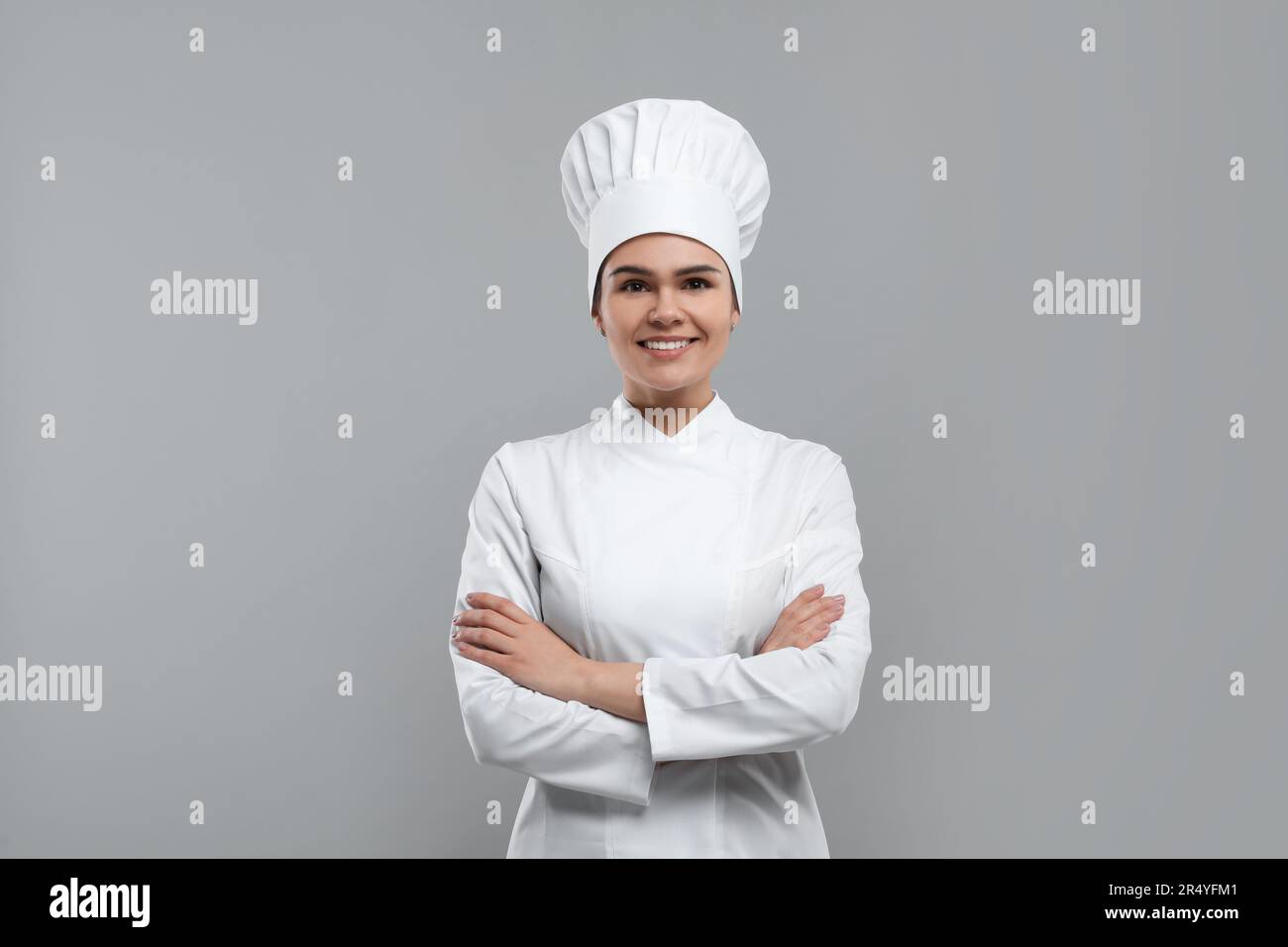 Happy female chef wearing uniform and cap on light grey background ...