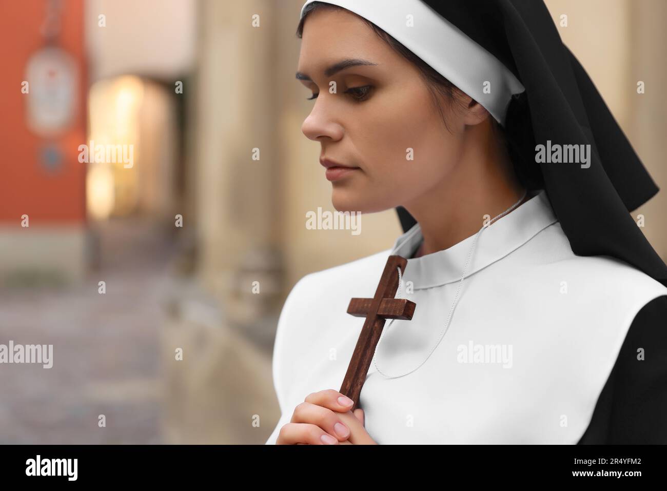 Young nun with Christian cross on city street, closeup. Space for text ...
