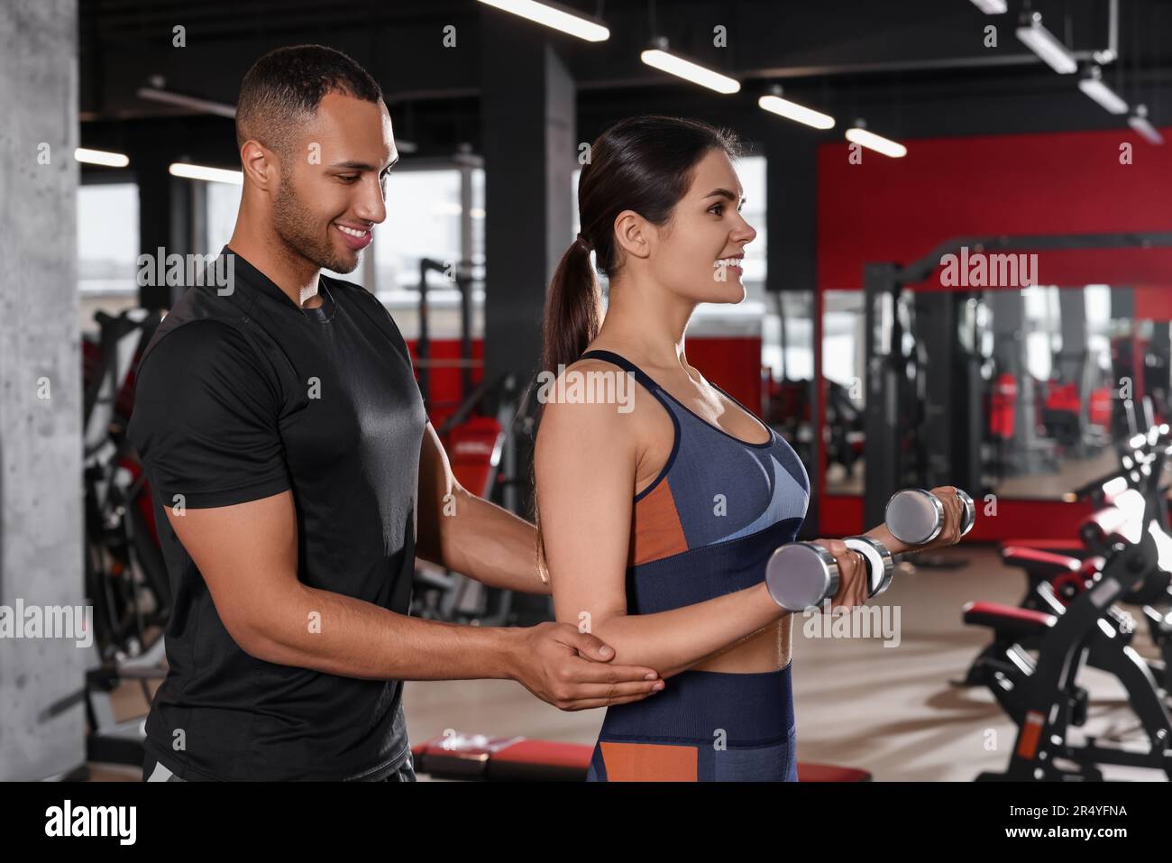 Happy trainer showing woman how to do exercise properly in modern gym ...