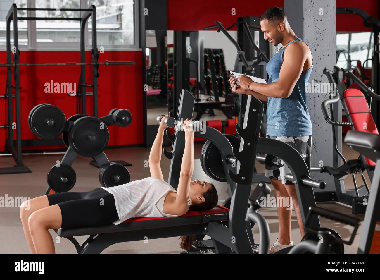 Trainer writing down plan of workouts while woman doing exercise in ...