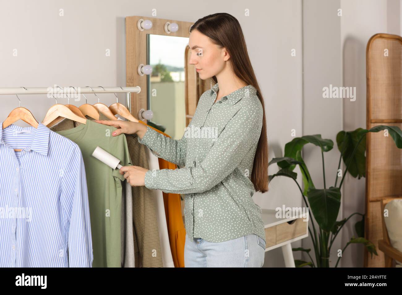 Young woman cleaning clothes with adhesive lint roller indoors Stock ...