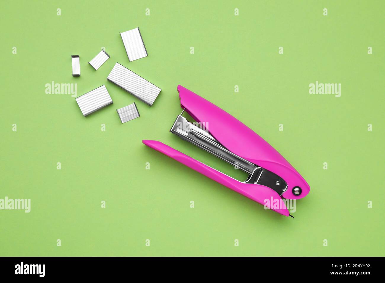 New bright stapler with staples on green background, fat lay. School ...