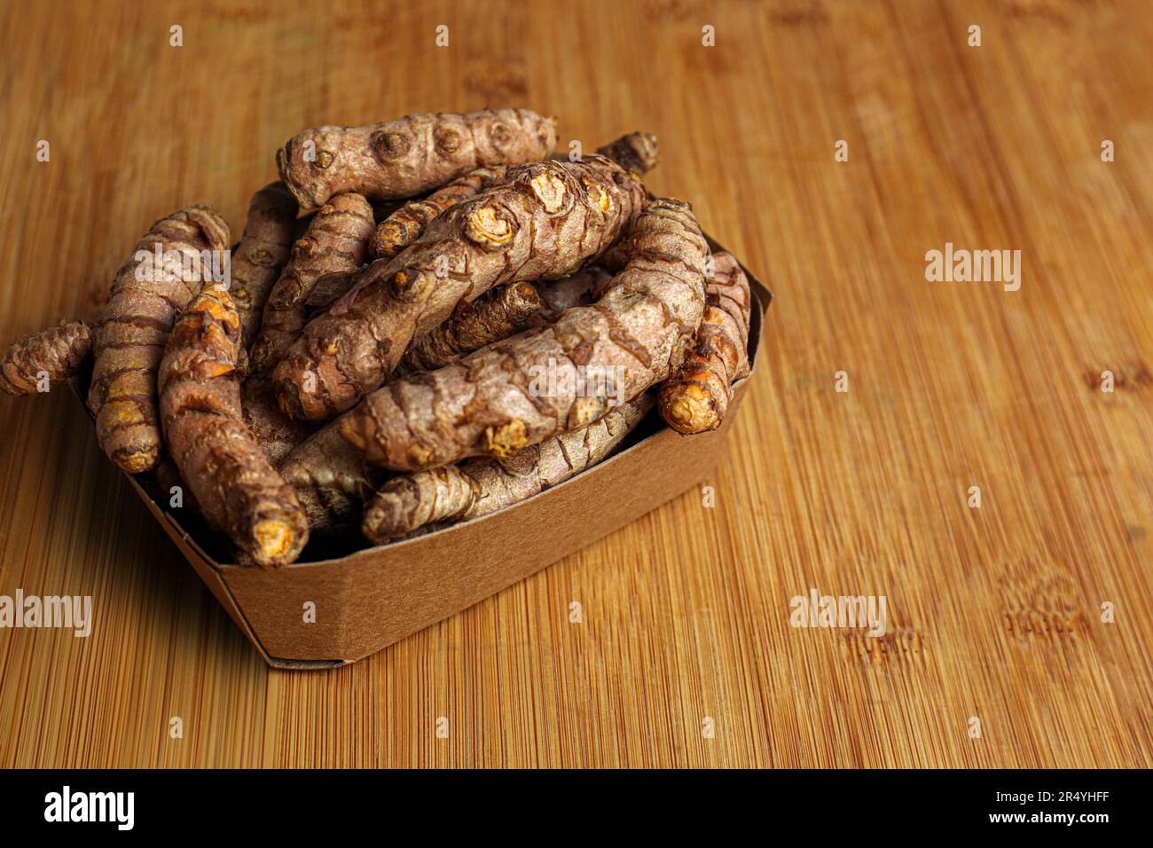 Cardboard box with whole turmeric roots on wooden table. Space for text ...