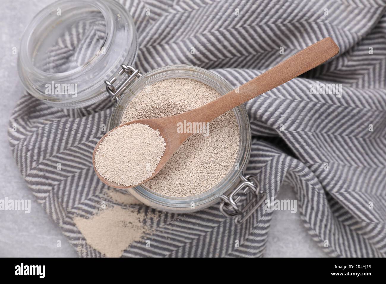 Glass jar and spoon with active dry yeast on light grey table, top view ...