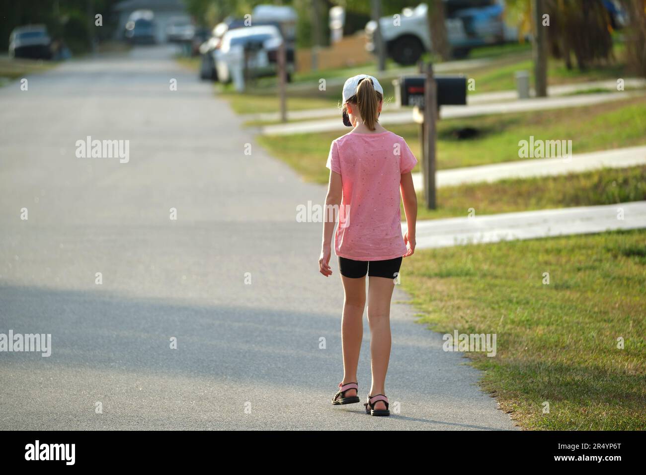 Back view of sad young child girl walking alone along the green street ...
