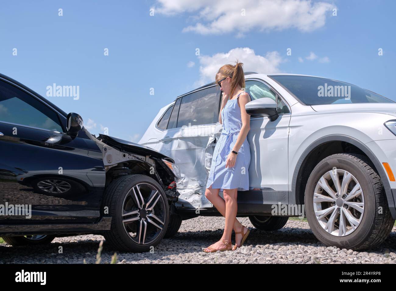 Sad young woman driver standing near her smashed car looking shocked on ...