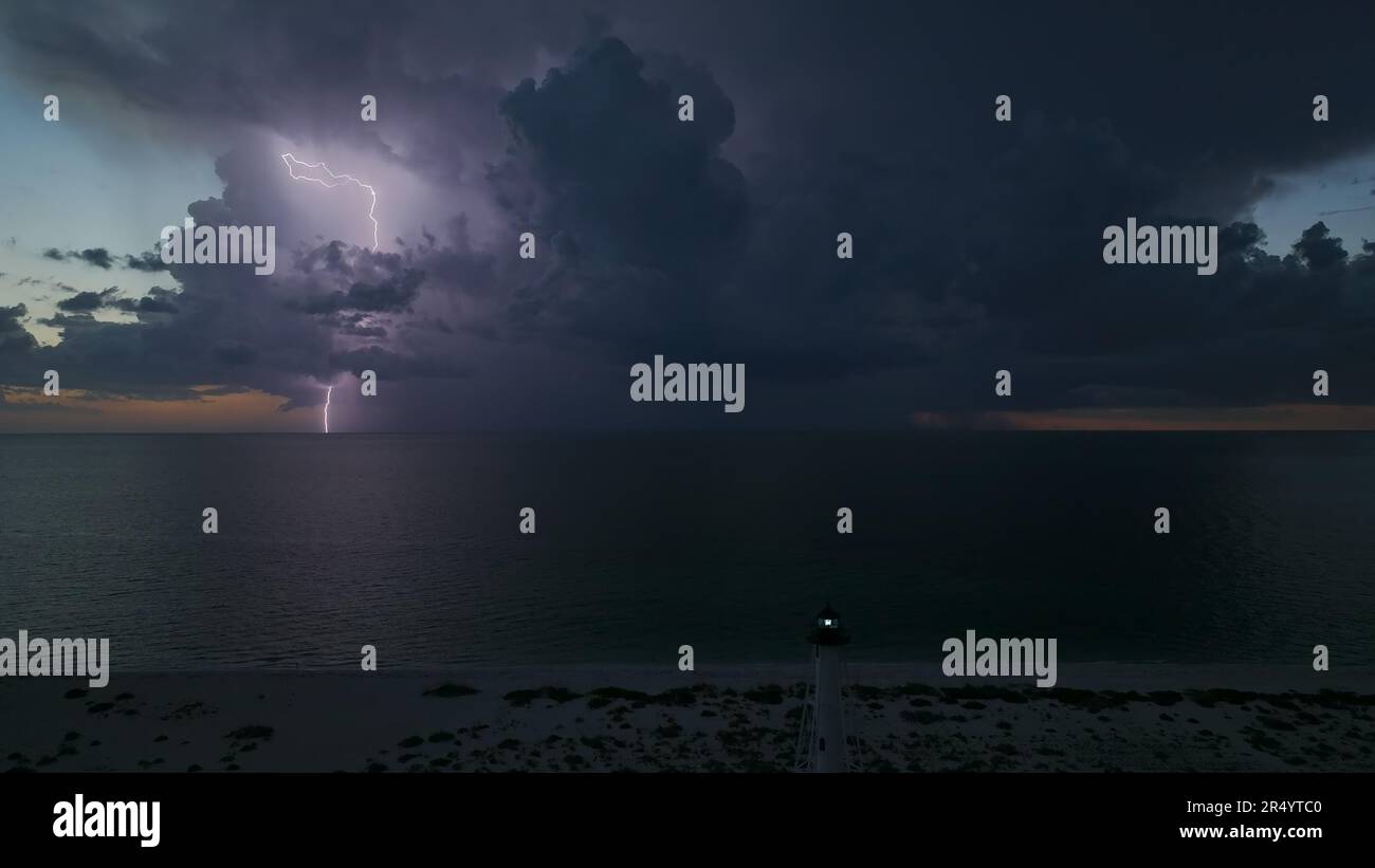 White tall lighthouse on sea shore with blinking light at stormy night ...