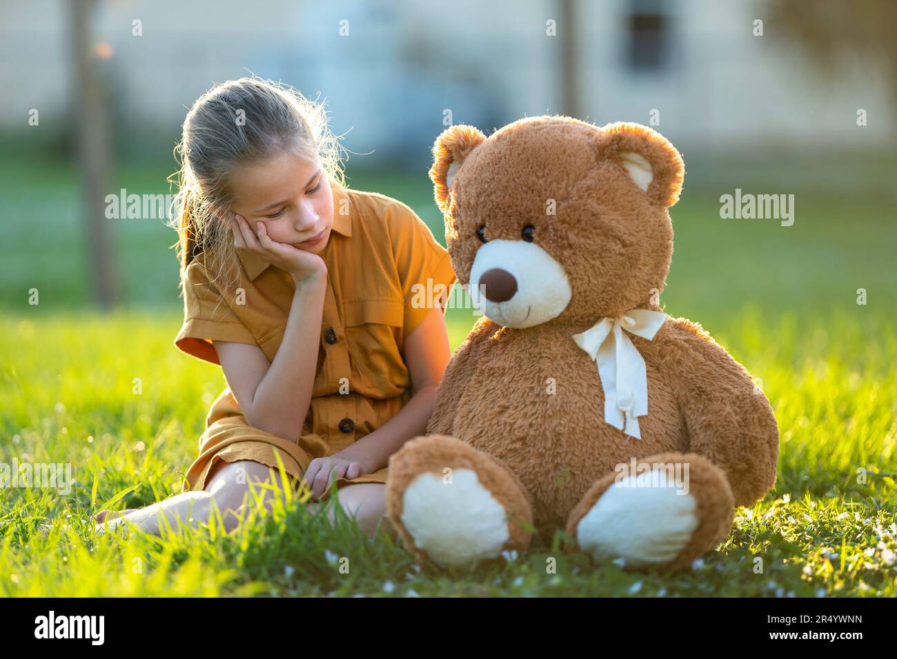 Unhappy child girl spending time with her teddy bear friend outdoors on sunny summer backyard ...