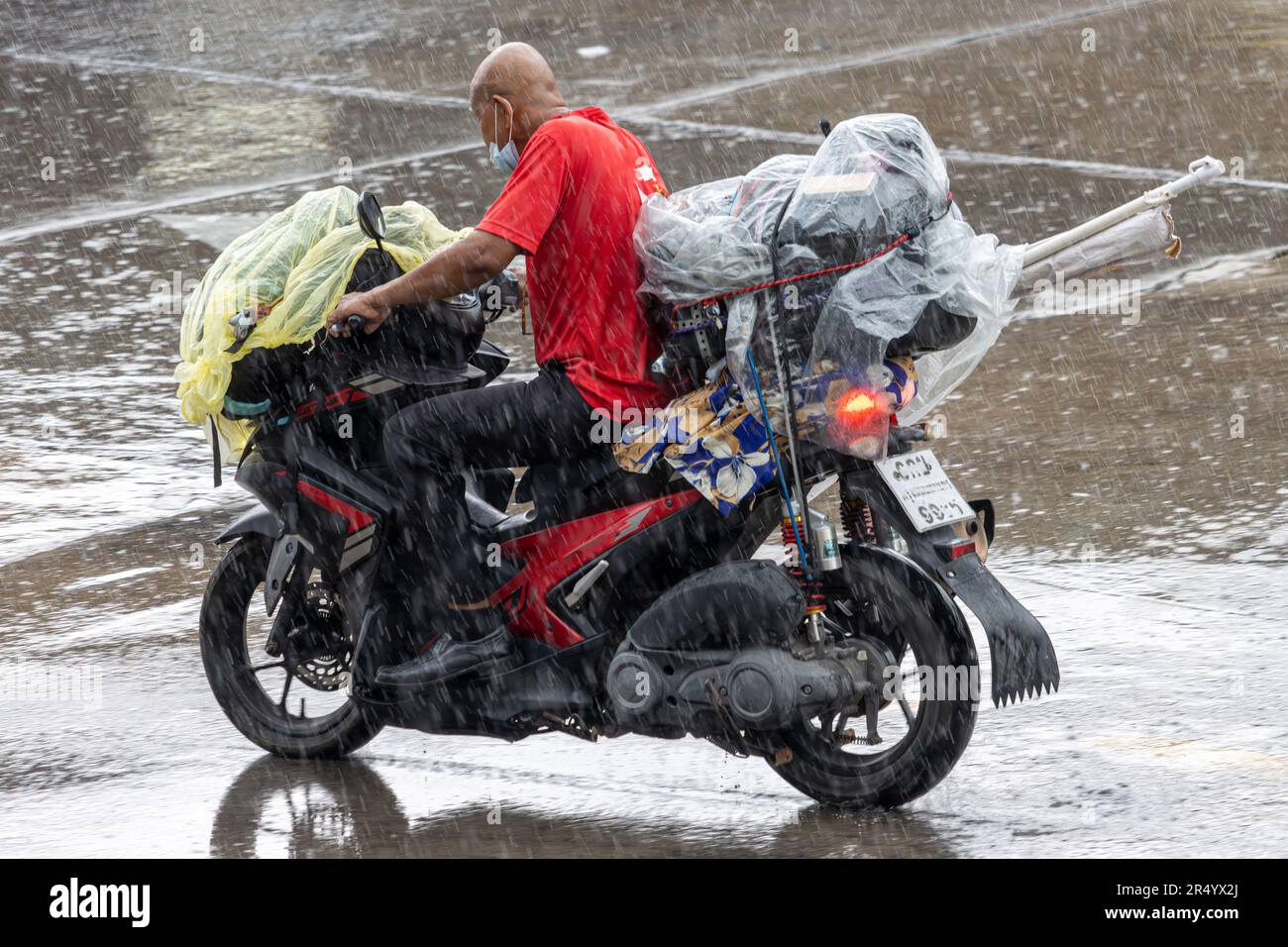 A man rides a motorcycle with a load in heavy rain Stock Photo - Alamy