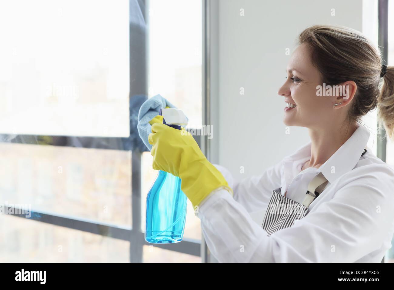 Cheerful maid sprays detergent on window glass in hotel room Stock ...