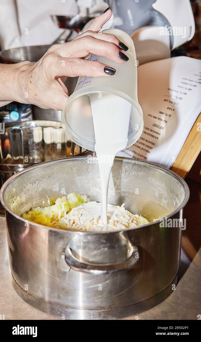 Chef in the home kitchen pours milk from measuring glass into pot with ...