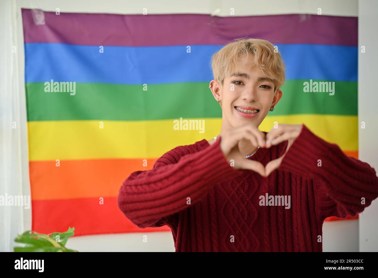 A smiling young Asian queer or gay man showed the heart hand sign while ...