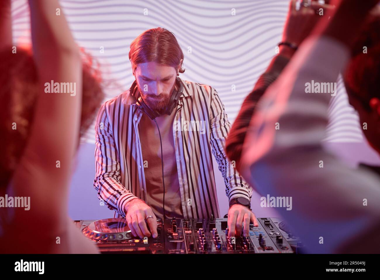 Portrait of long haired DJ by turntable in neon lights entertaining ...