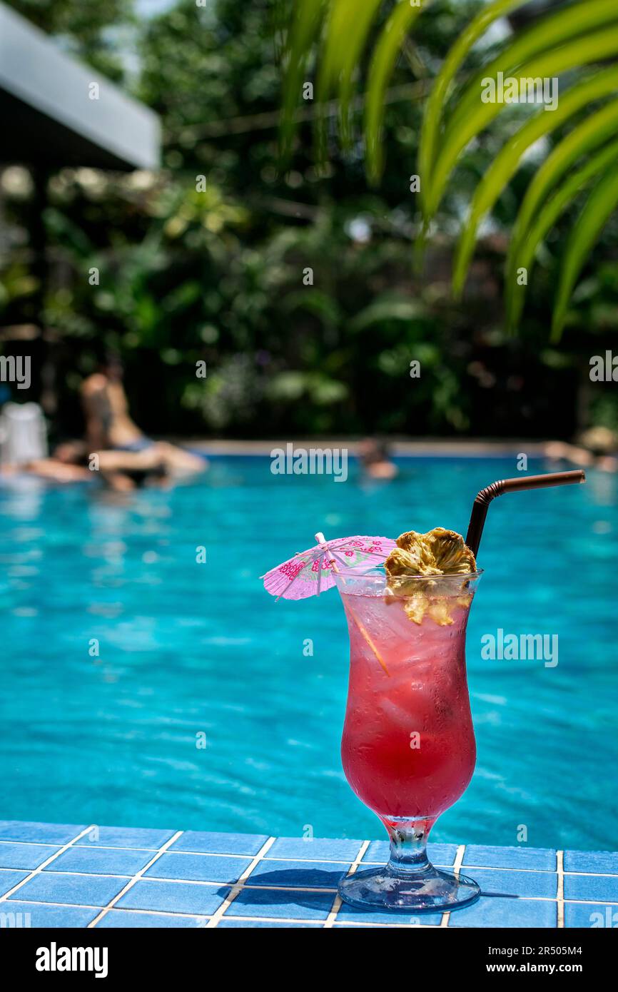 tropical Singapore sling cocktail in tall glass by resort swimming pool ...