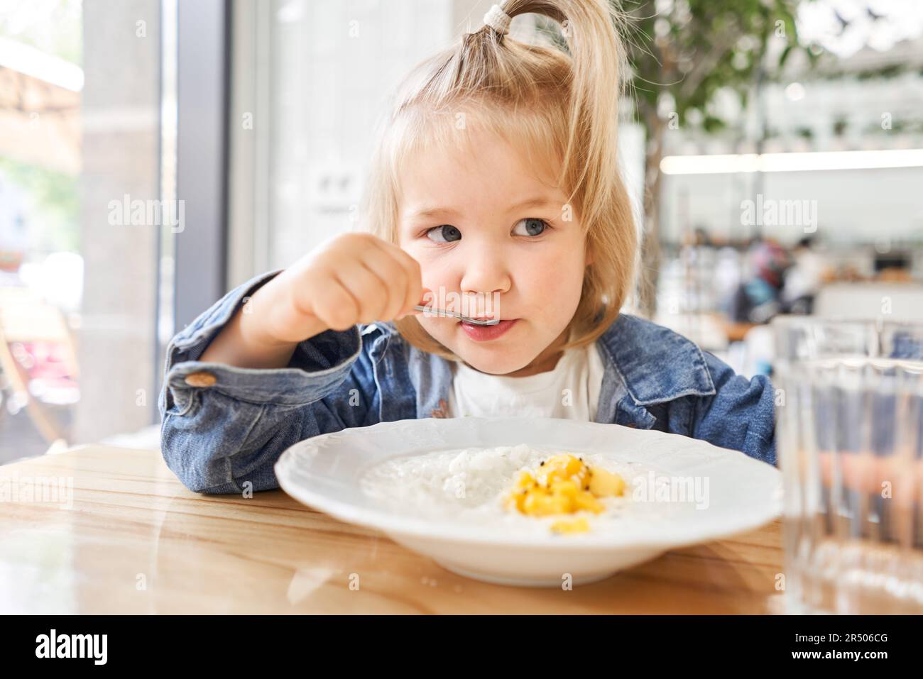 Adorable girl drinking still water, eating rice porridge with mango ...