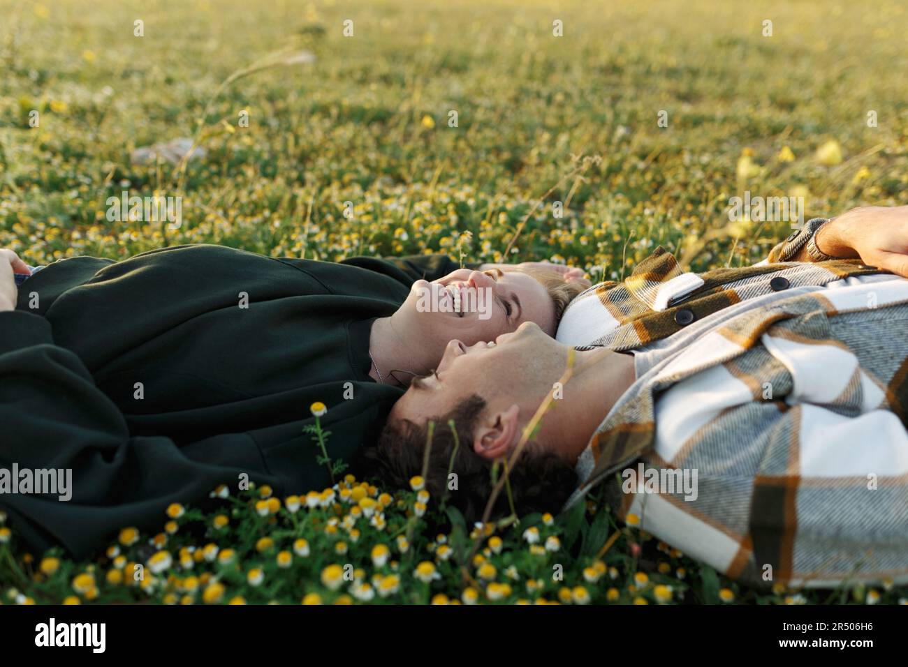 Side view of relaxed young couple lying together on green grass with ...