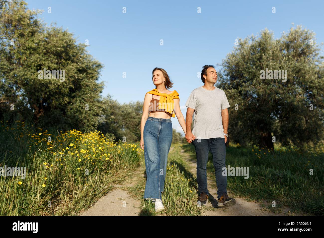 Outdoor shot of young couple in love walking on pathway through grass ...