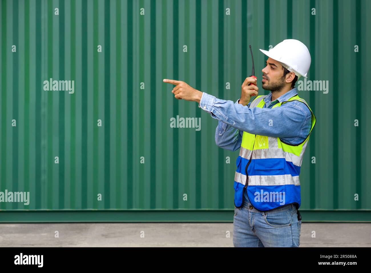 Young shipment worker with safety vest and hardhat pointing at ...