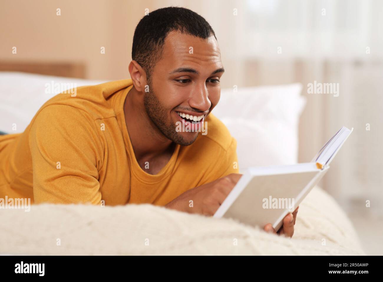 Happy African American man reading book on bed at home Stock Photo - Alamy