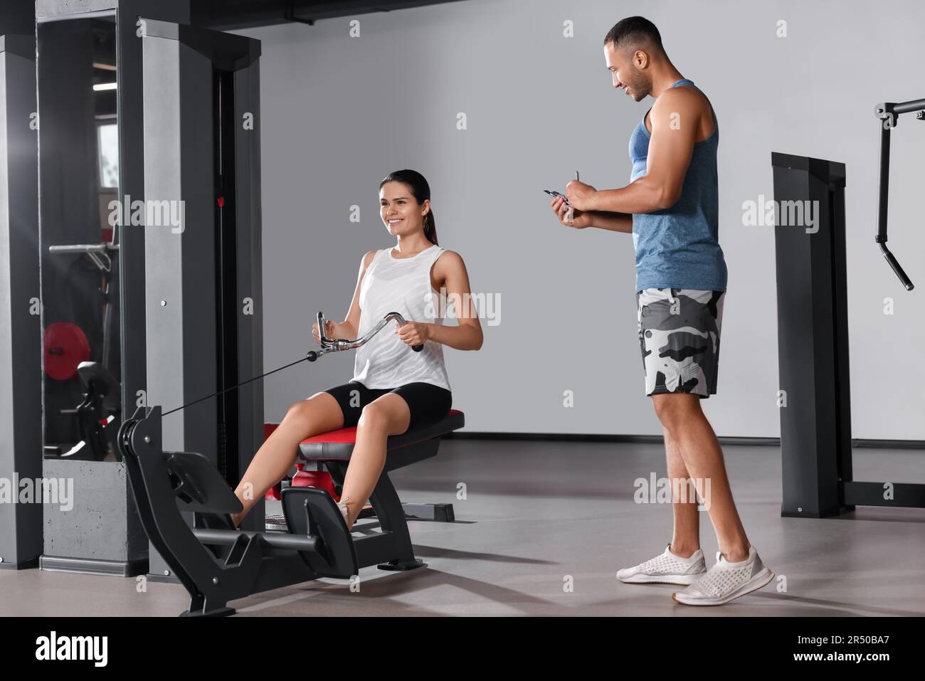 Happy trainer writing down plan of workouts while woman doing exercise ...