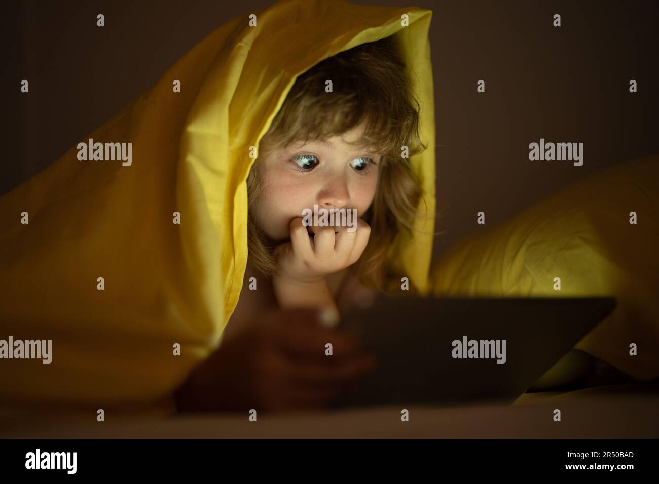 Kid boy lying on bed and surfing Internet on tablet in dark room. Child ...
