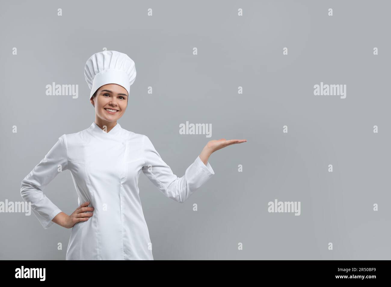 Happy female chef pointing at something on light grey background. Space ...