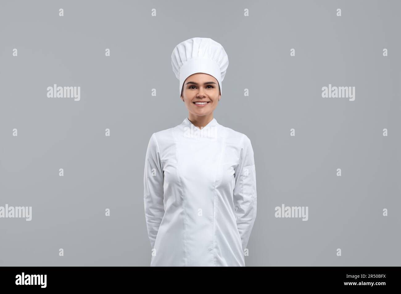 Happy female chef wearing uniform and cap on light grey background ...