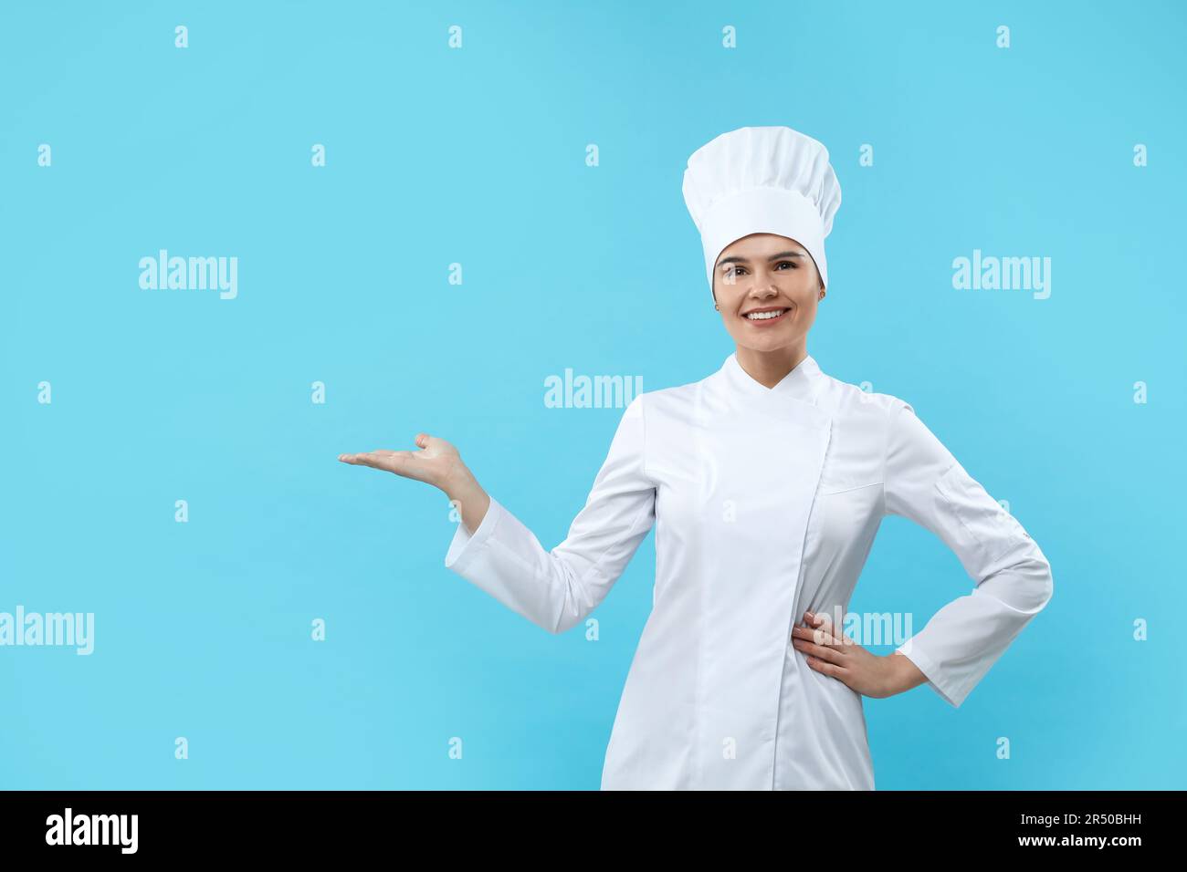 Happy female chef wearing uniform and cap on light blue background ...