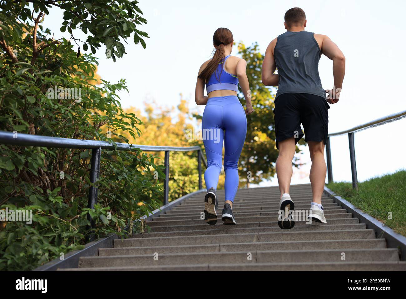 Sporty couple running up stairs outdoors on sunny day, back view Stock ...