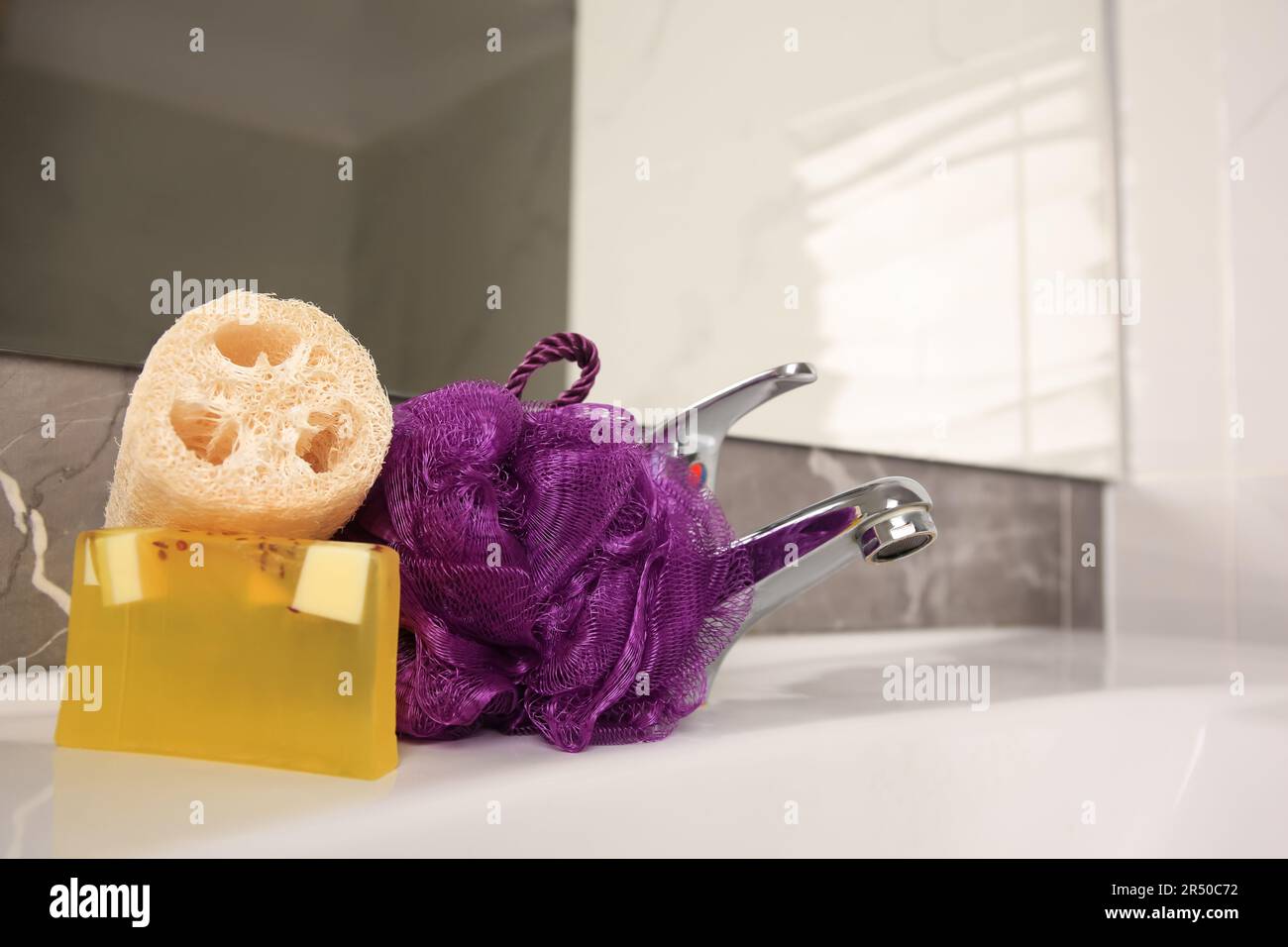Purple shower puff, loofah sponge and soap on sink in bathroom, space ...