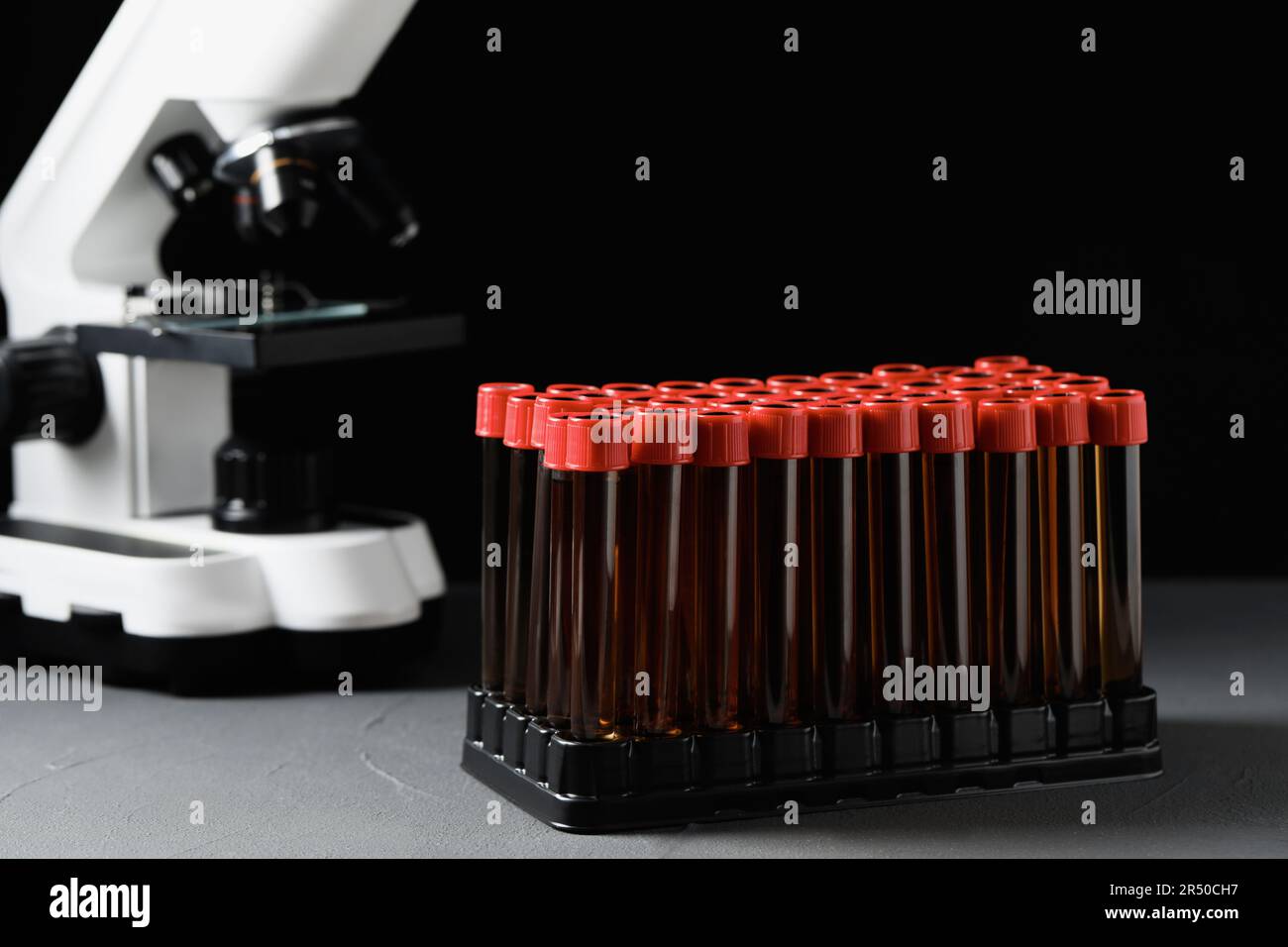 Test tubes with brown liquid in stand on grey table against black ...