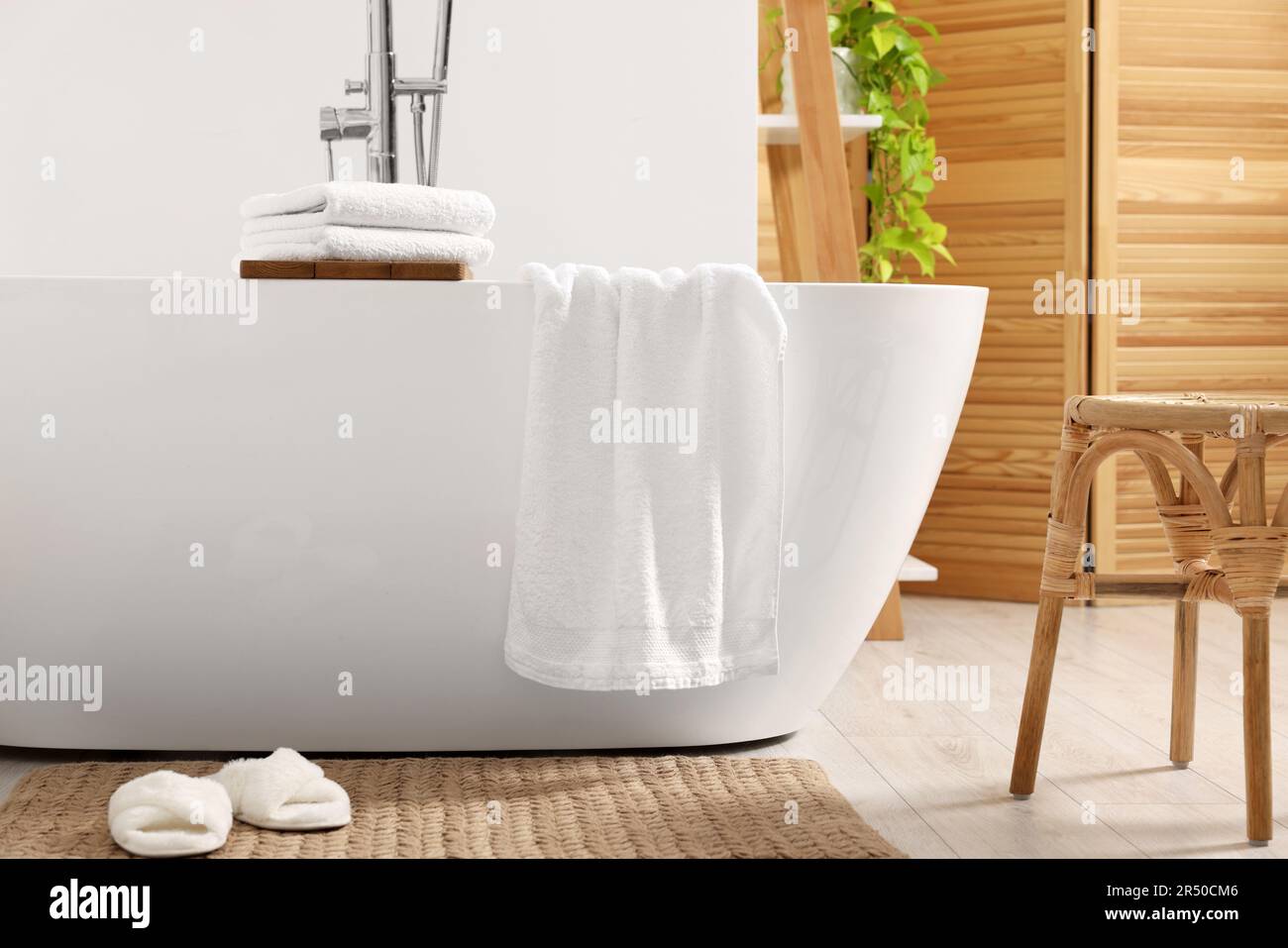 Stylish tub, wicker stool, slippers and soft towels in bathroom Stock ...