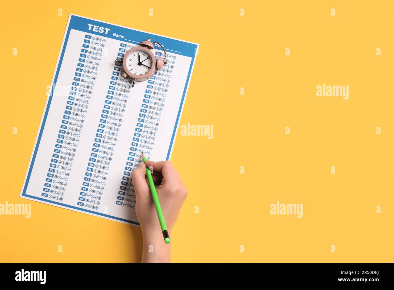Student filling answer sheet on yellow background, top view with space ...