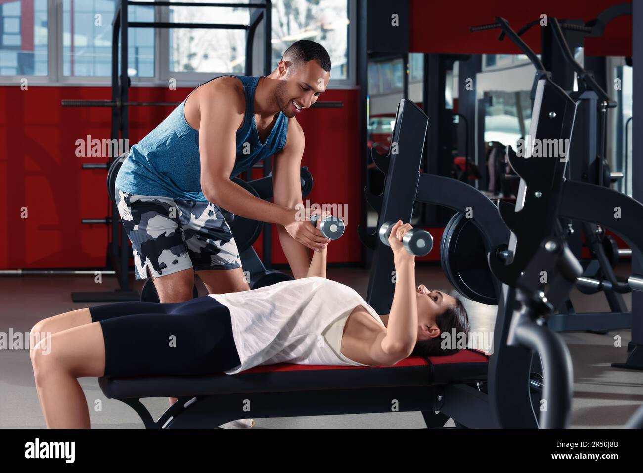 Happy trainer showing woman how to do exercise properly in modern gym ...