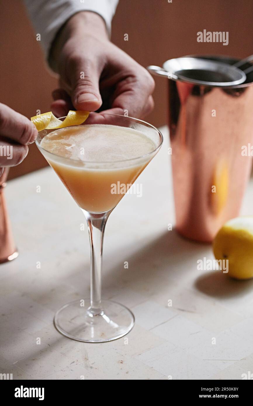 A whisky sour cocktail with lemon garnish being added to the glass ...