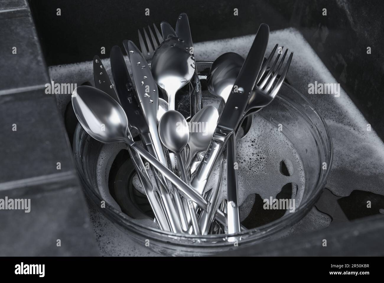 Washing silver spoons, forks and knives in kitchen sink with foam ...