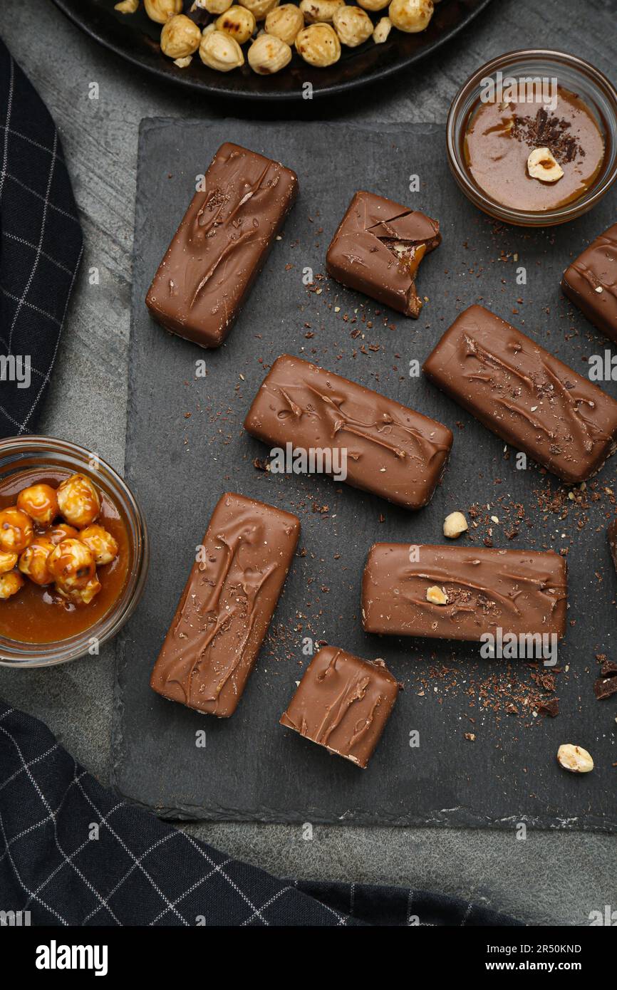 Delicious chocolate candy bars with caramel and nuts on grey table ...
