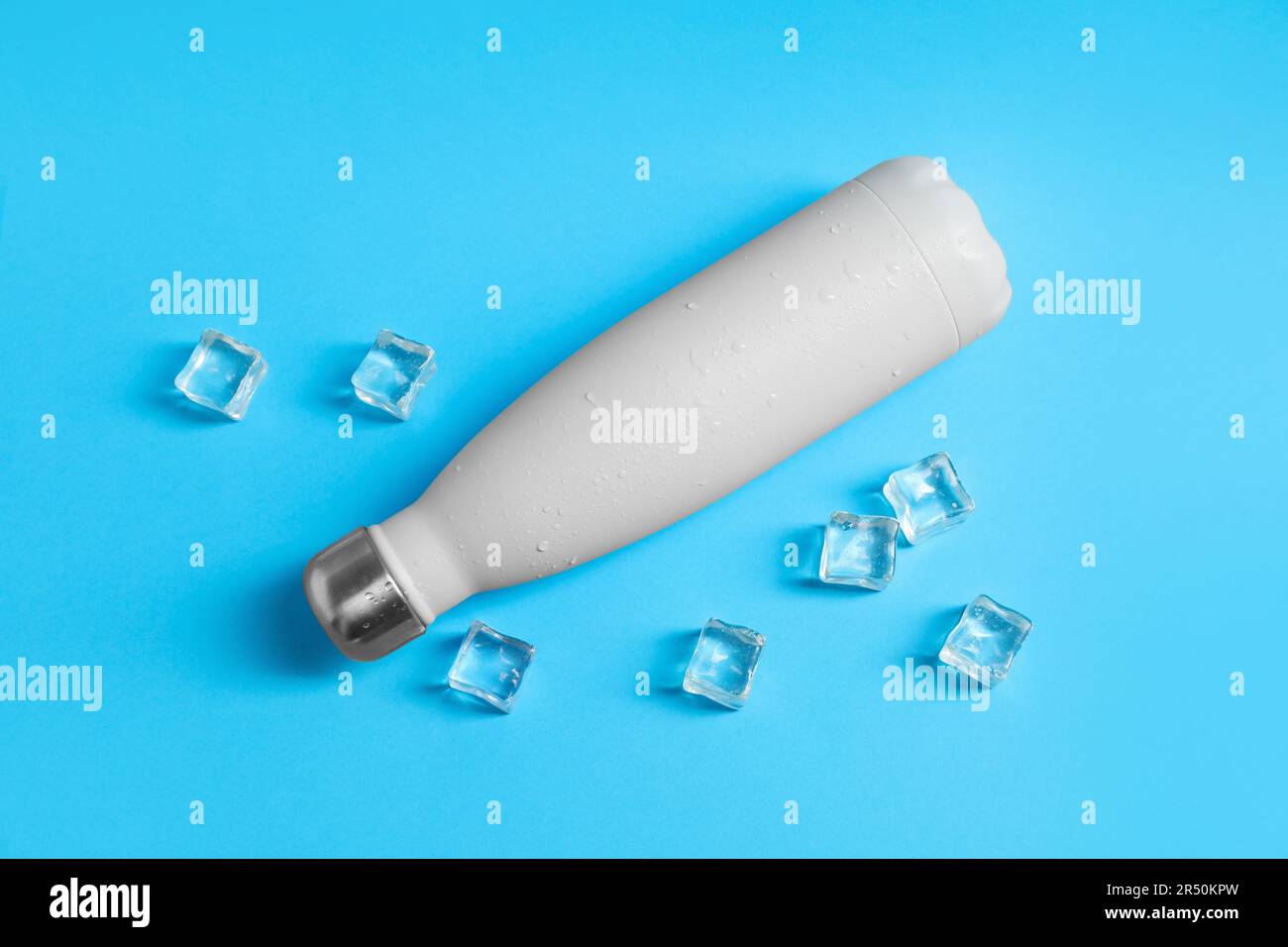 Stylish thermo bottle with water drops and ice cubes on light blue ...