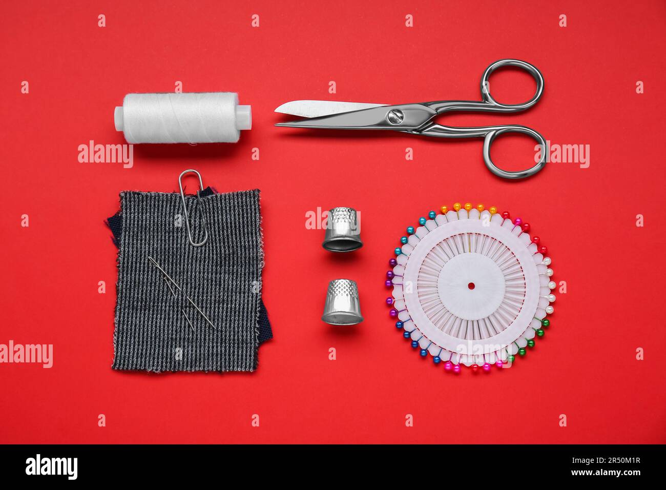 Flat lay composition with thimbles and different sewing tools on red ...