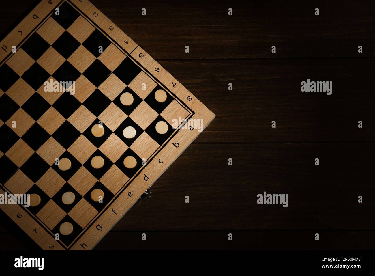 Checkerboard with game pieces on wooden table, top view. Space for text ...