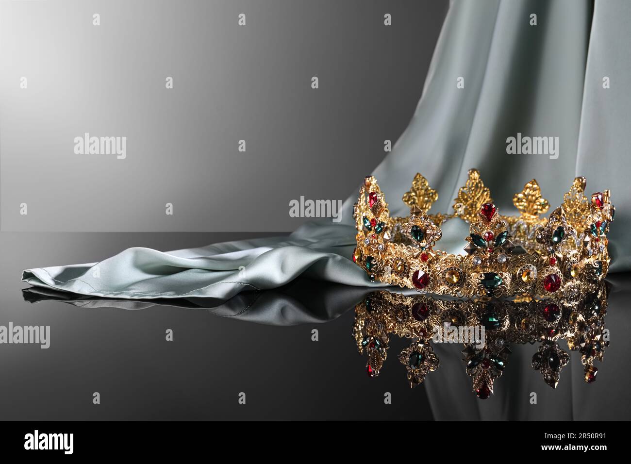 Beautiful golden crown with gems near light cloth on dark mirror ...