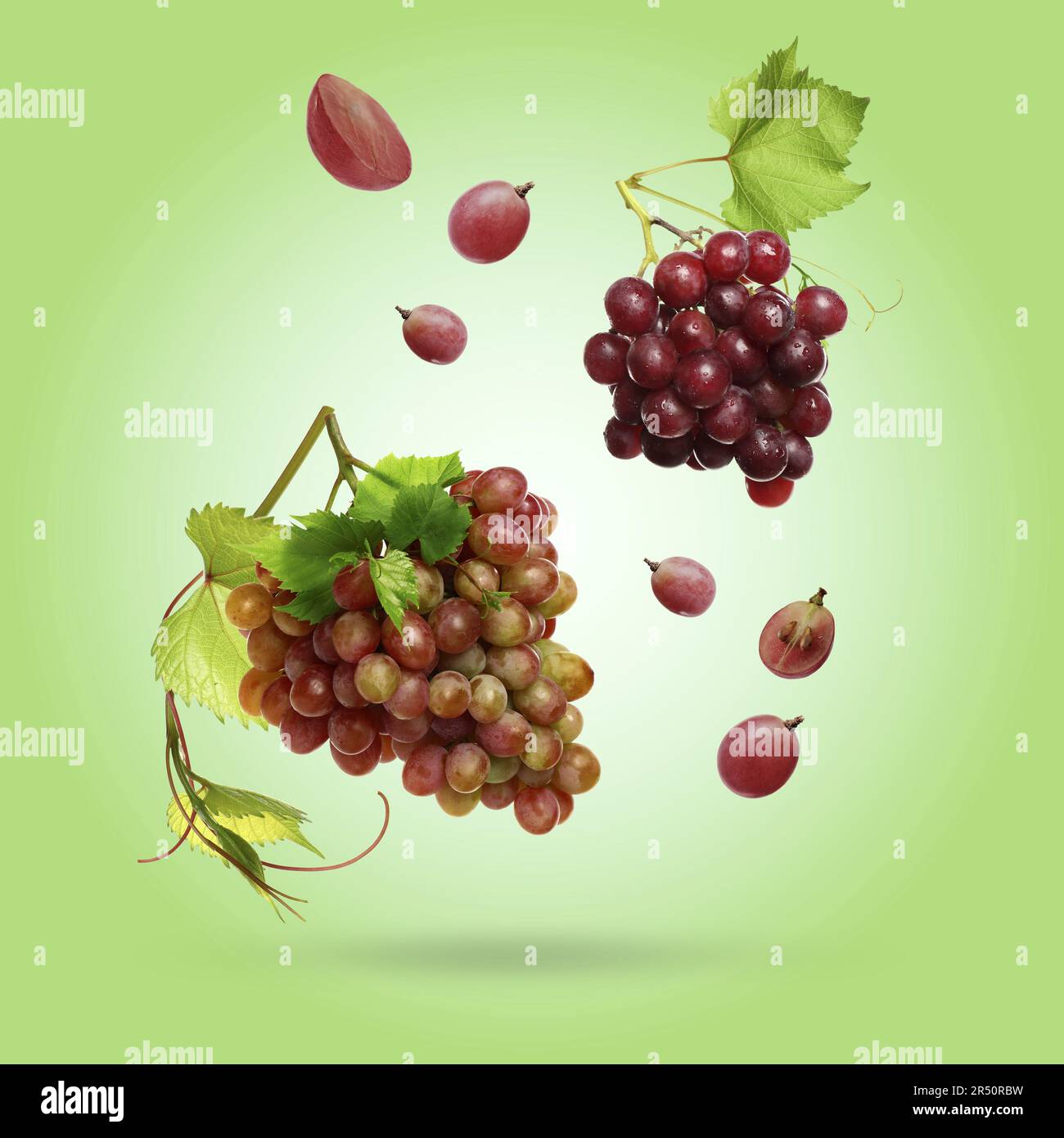 Delicious fresh red grapes and leaves falling on light green background ...