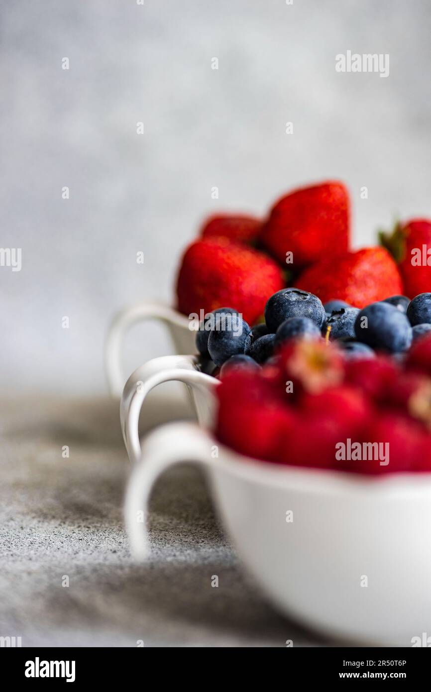 Strawberries, blueberries, and raspberries in small bowls on a concrete ...