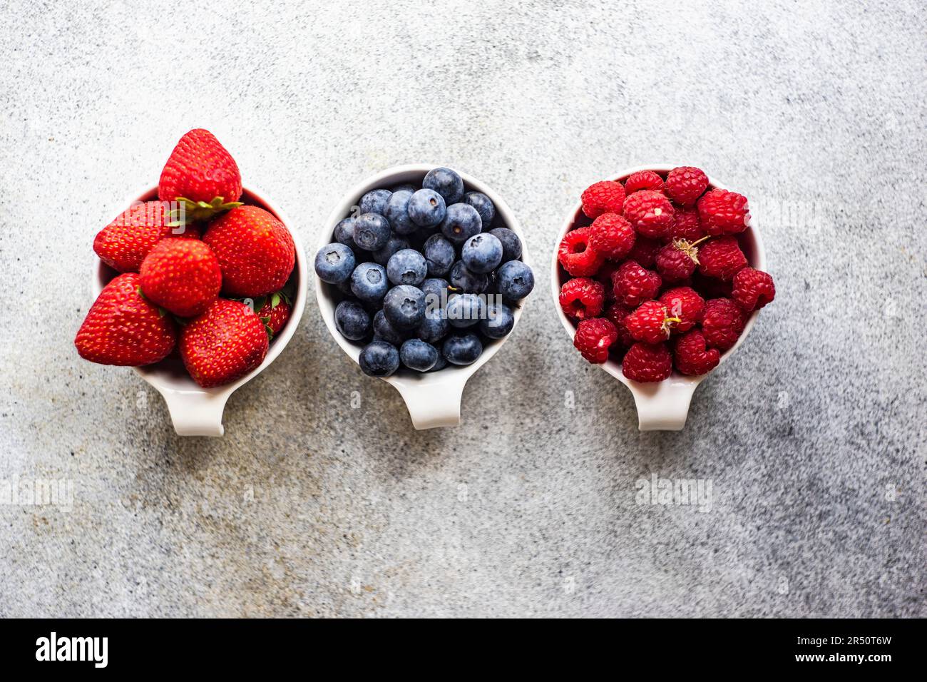 Strawberries, blueberries, and raspberries in small bowls on a concrete ...