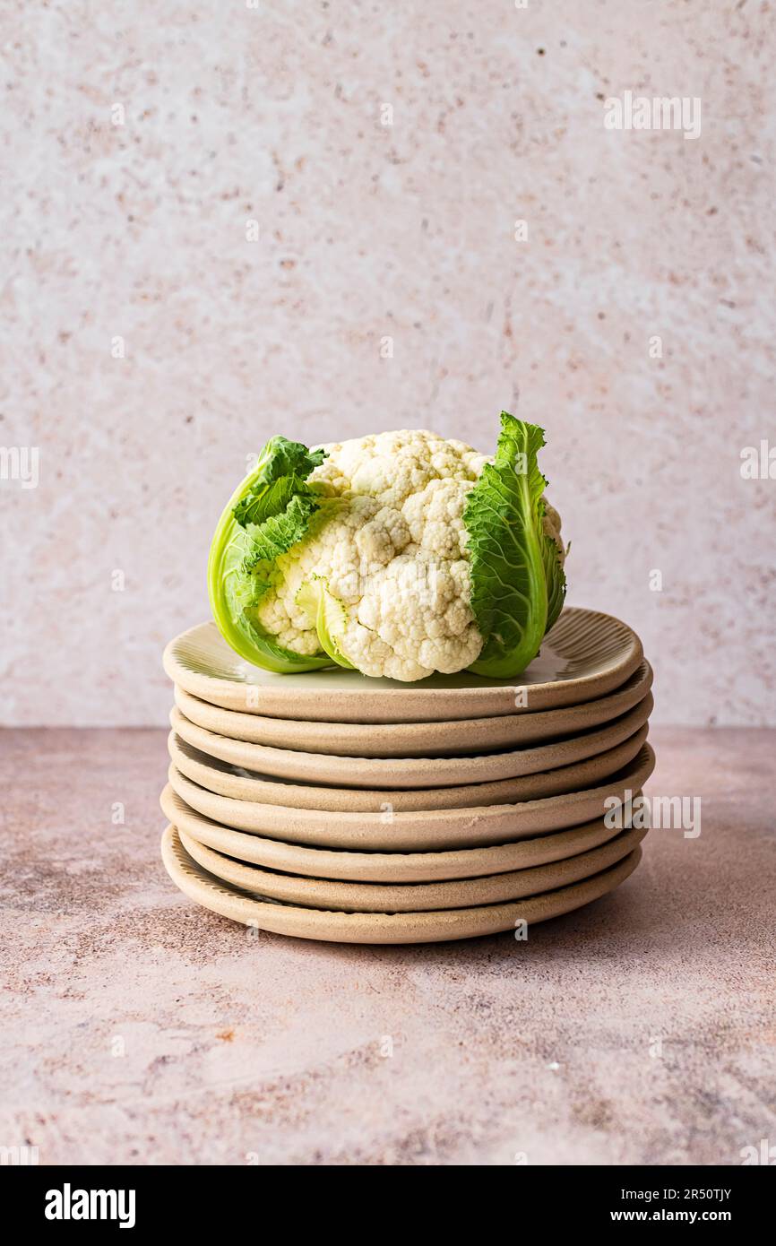 Organic cauliflower with leaves on a stack of fluted ceramic plates ...
