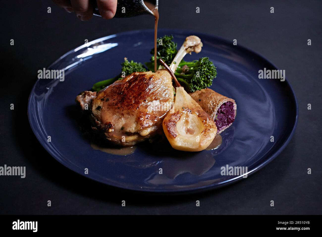 Duck leg served with pear and au jus on a blue plate Stock Photo - Alamy