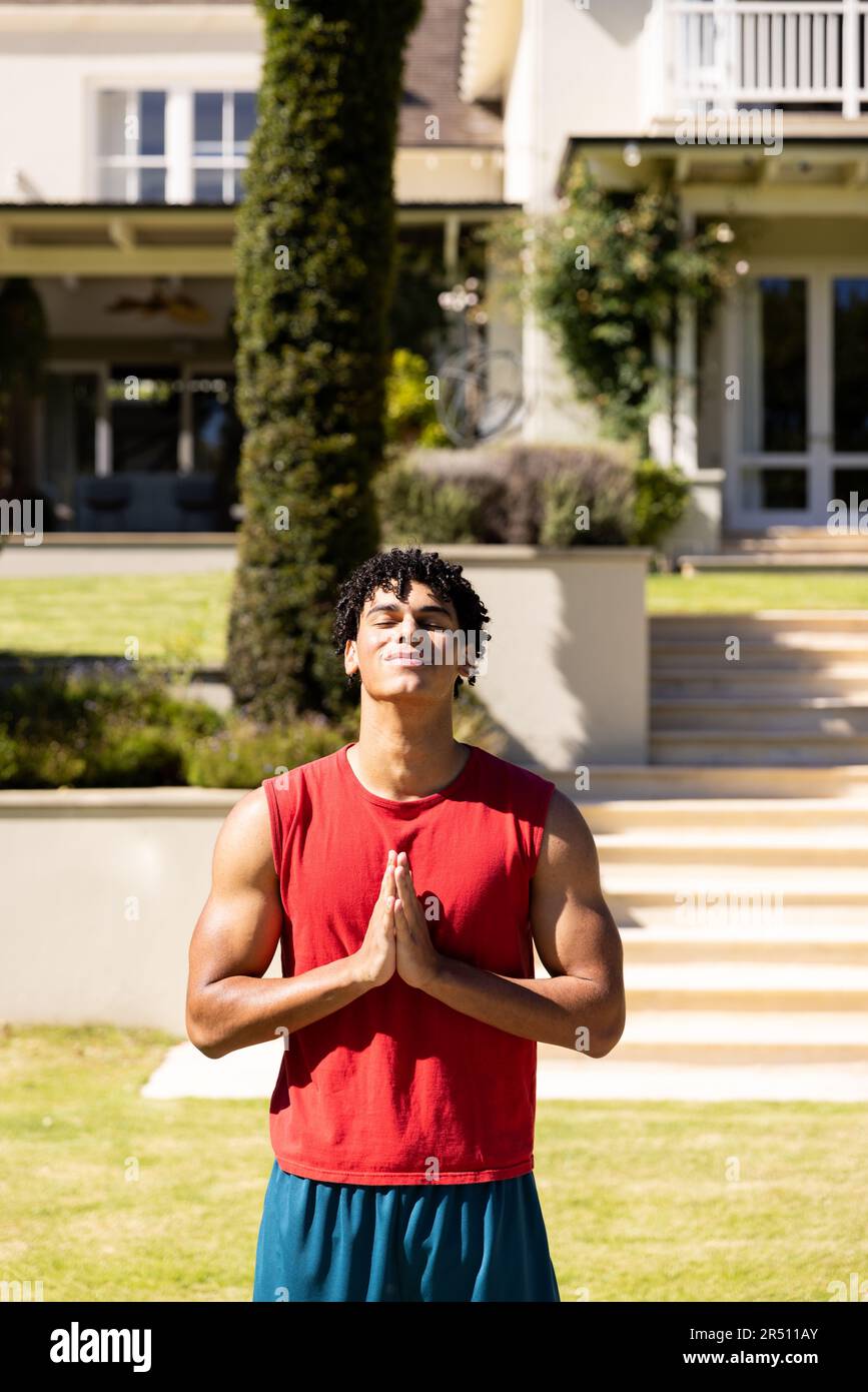 Biracial handsome young man with eyes closed meditating in prayer pose ...