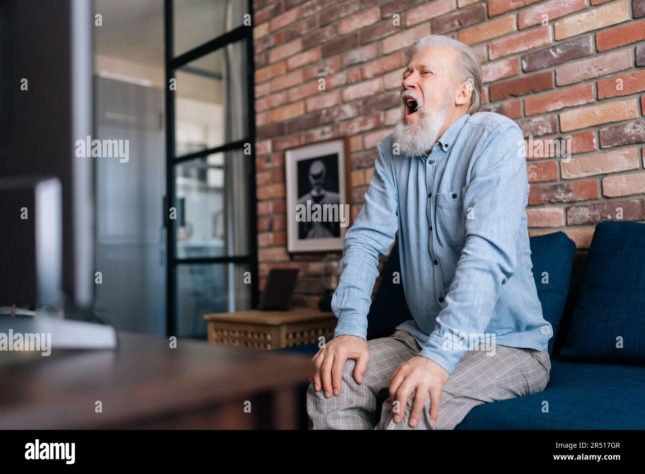 Happy excited grey-haired mature football fan sitting at TV screen and ...